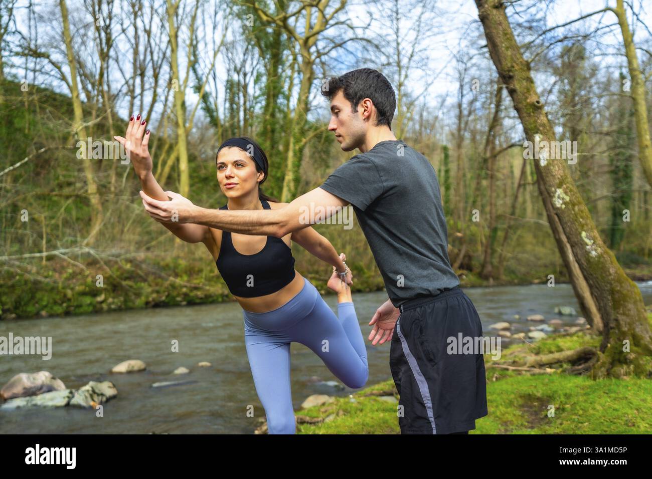 Yoga instructor helping a student performing a balancing pose next to a ...