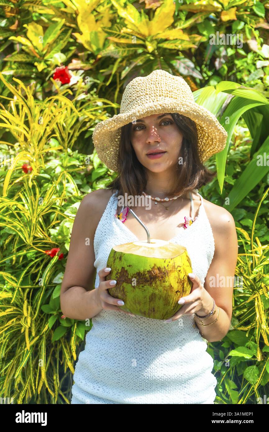 Young woman wearing straw hat holding fresh green coconut with metal ...