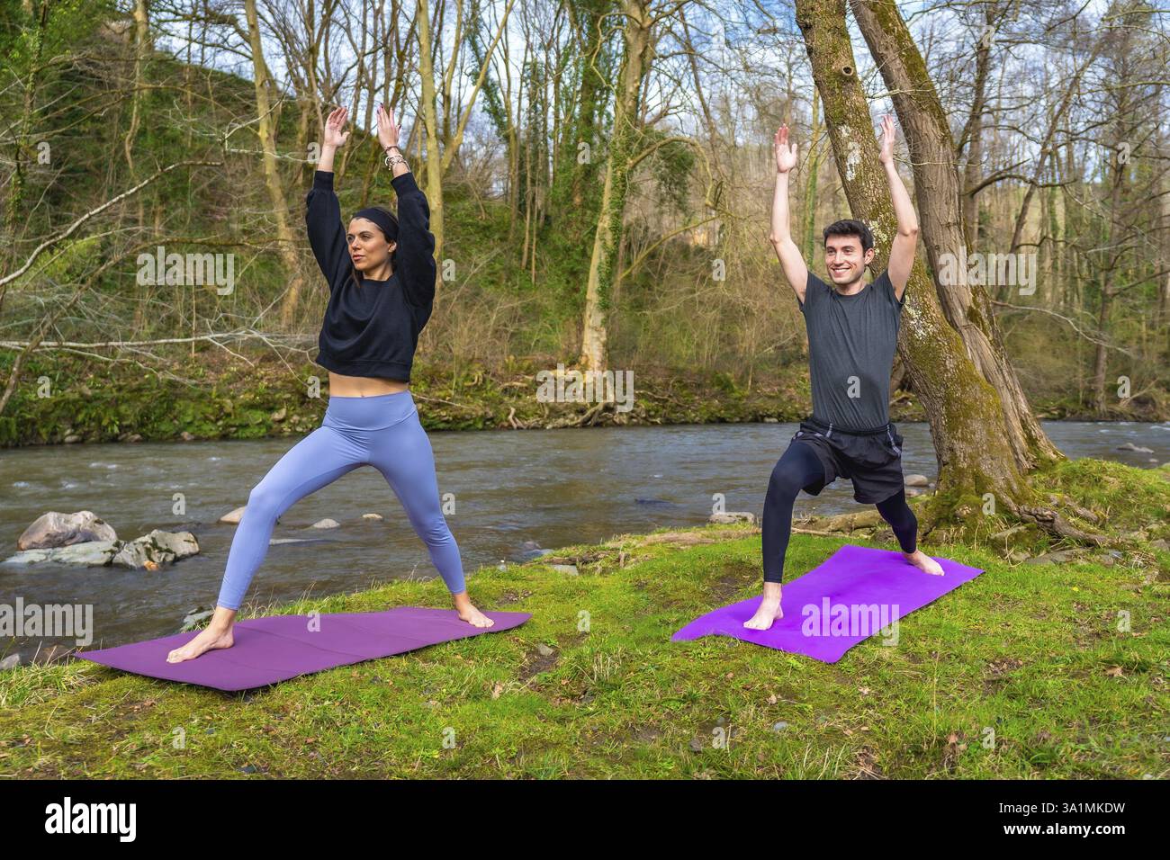 Man and woman practicing yoga by a river in nature, performing the ...
