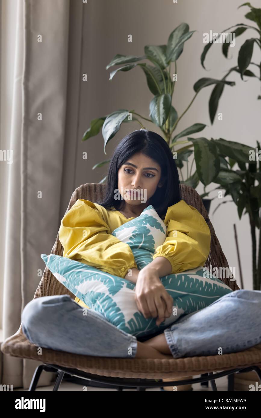 Sad woman hugging pillow while sitting curled up in chair Stock Photo ...