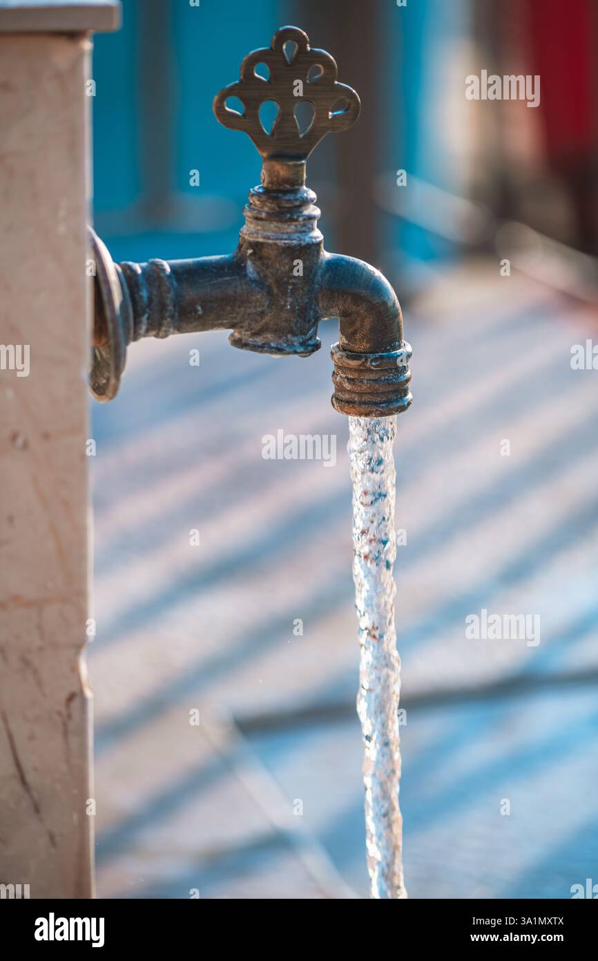 Water flows from an ornate outdoor faucet mounted on a stone pillar ...