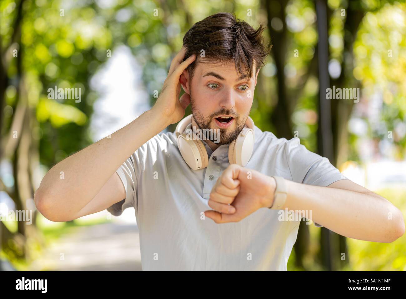 Happy active man runner jogging in city park and looking at smartwatch ...