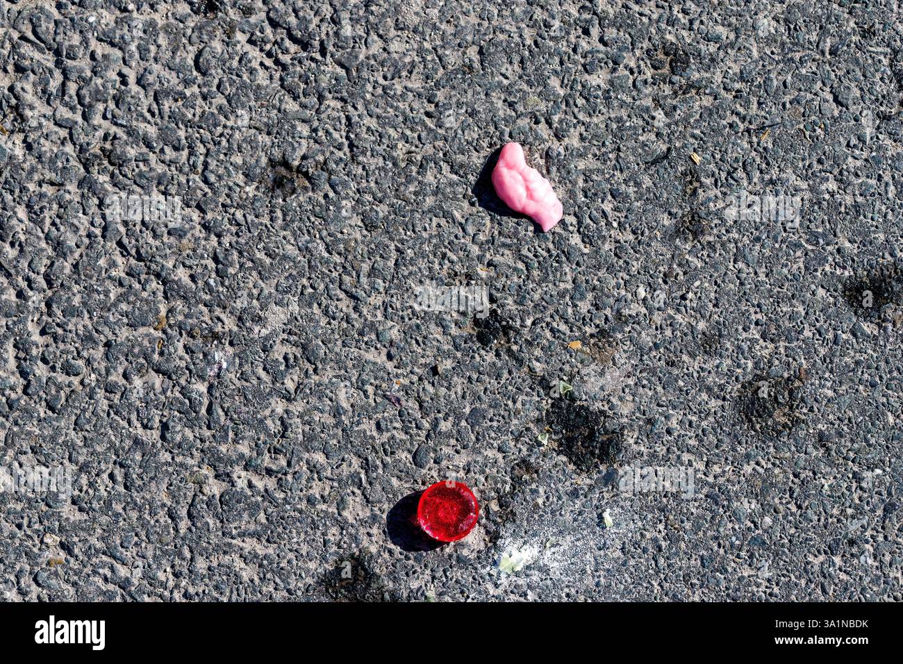 Asphalt surface shows a pink piece of gum, a red round object, and ...