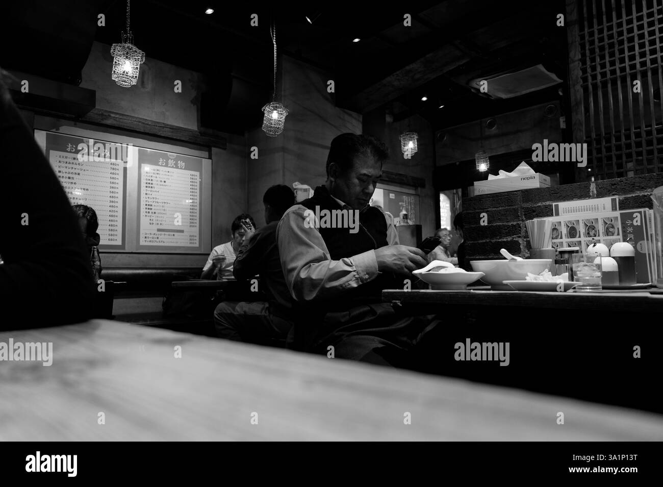 Middle aged man dining alone in a cozy izakaya, captured in black and ...