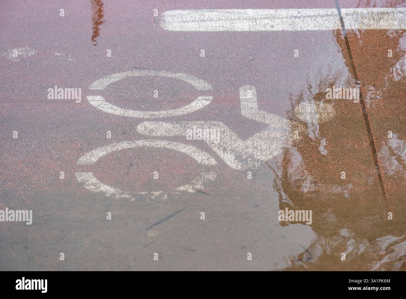 A wet road with a bike symbol in the middle. The bike symbol is white ...