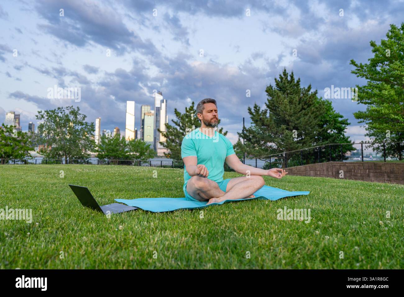 Sport Man meditating in lotus pose in grass outdoors. Sportsman doing ...