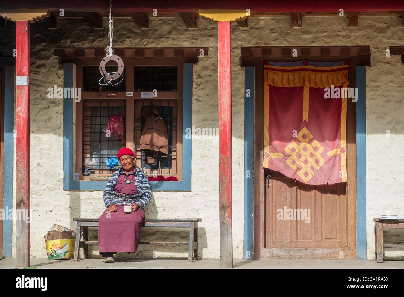 Elderly lady sits peacefully in front of Satya Monastery (Nar Phedi Gompa) on a sunny day in Nar ...
