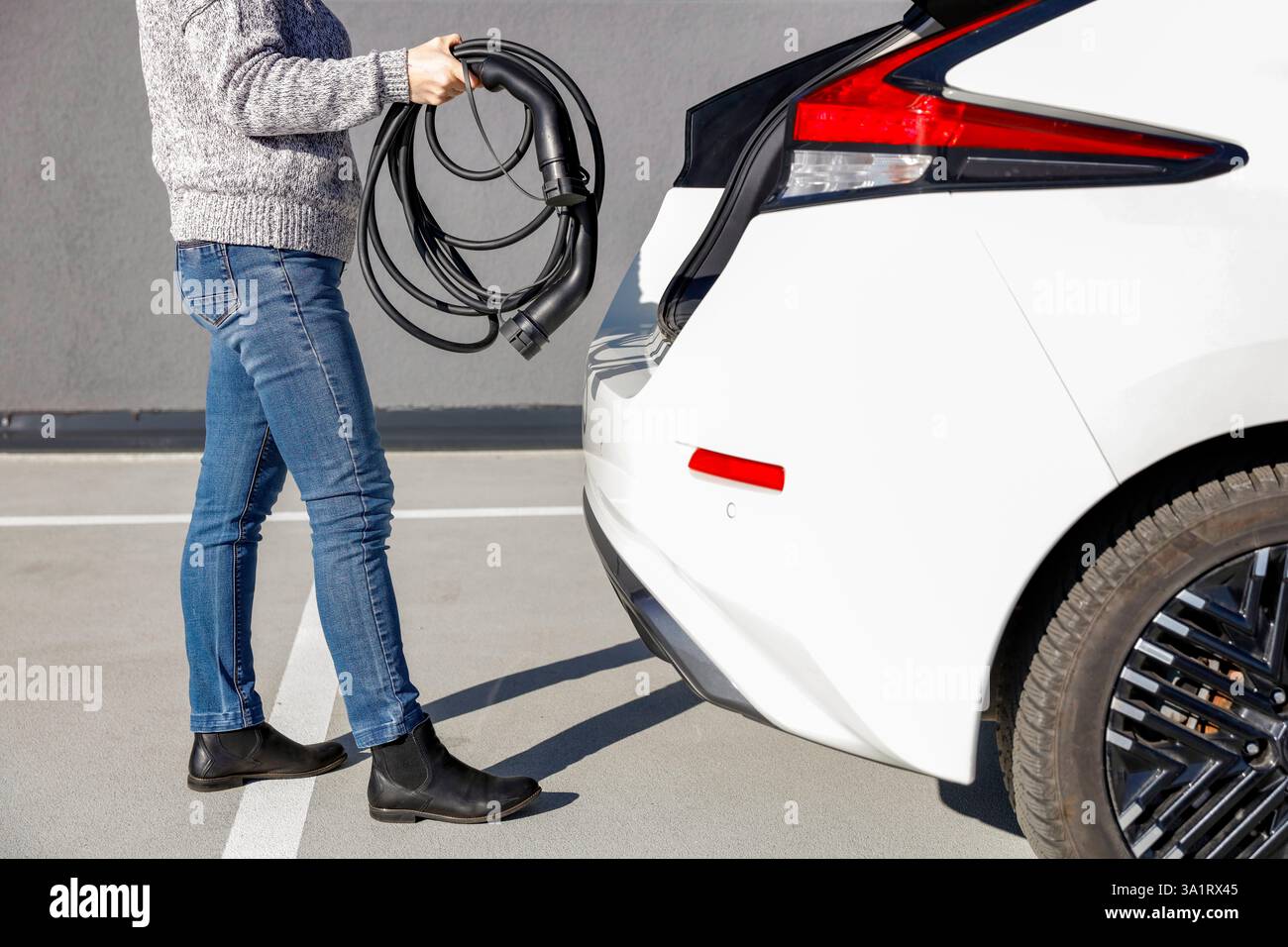 Woman holding coiled electric car charging cable near a white car in ...