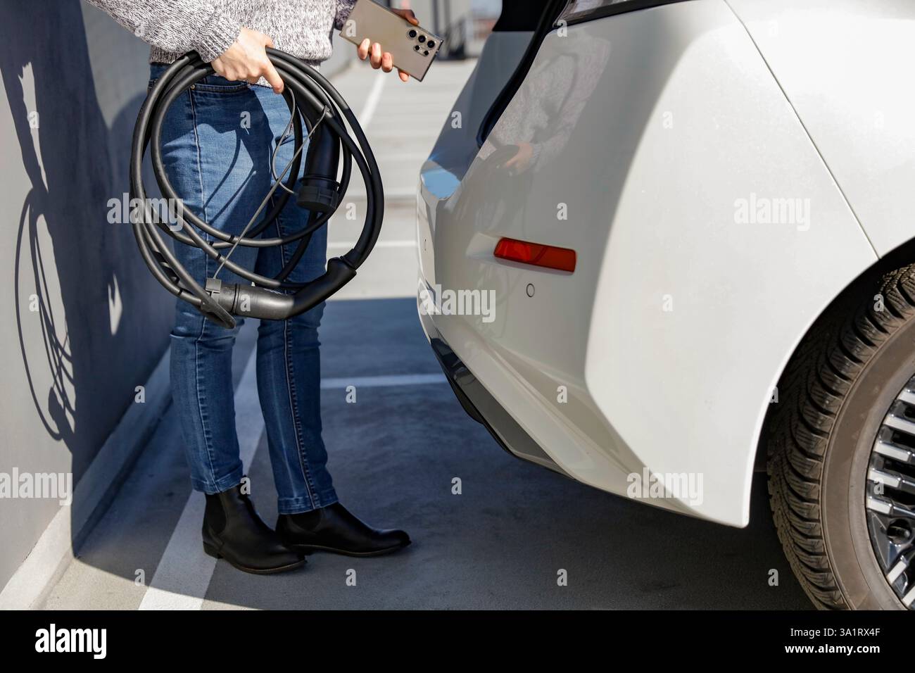 Woman holding coiled electric car charging cable near a white car in ...