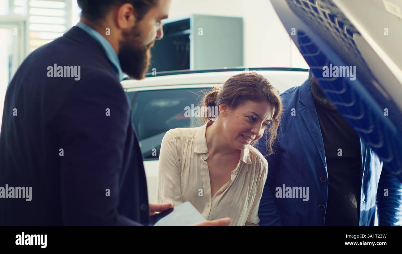 Salesman showing components under car hood to customers, hoping to ...
