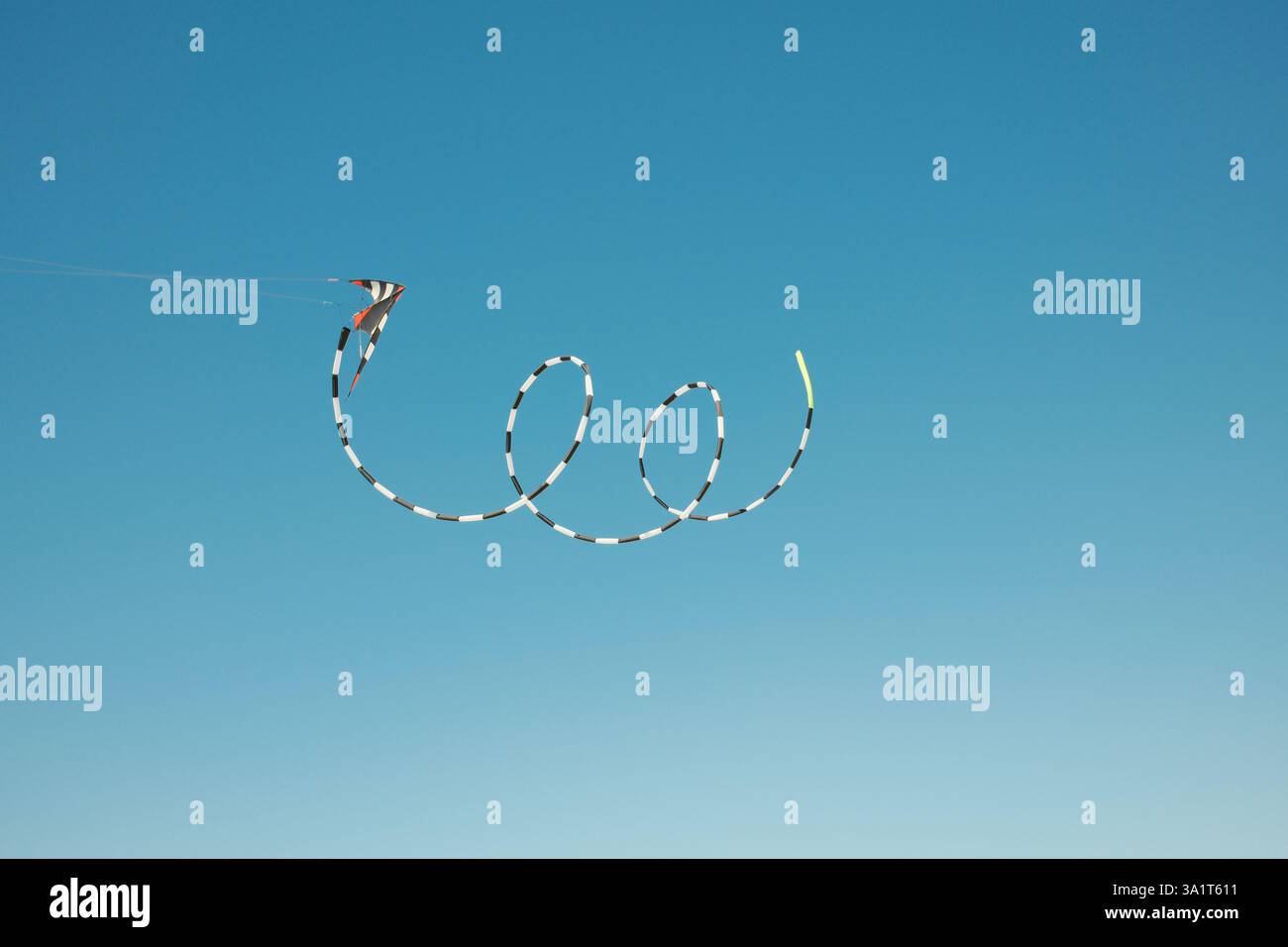 Kite flying high in the clear blue sky with long checkered tail Stock ...