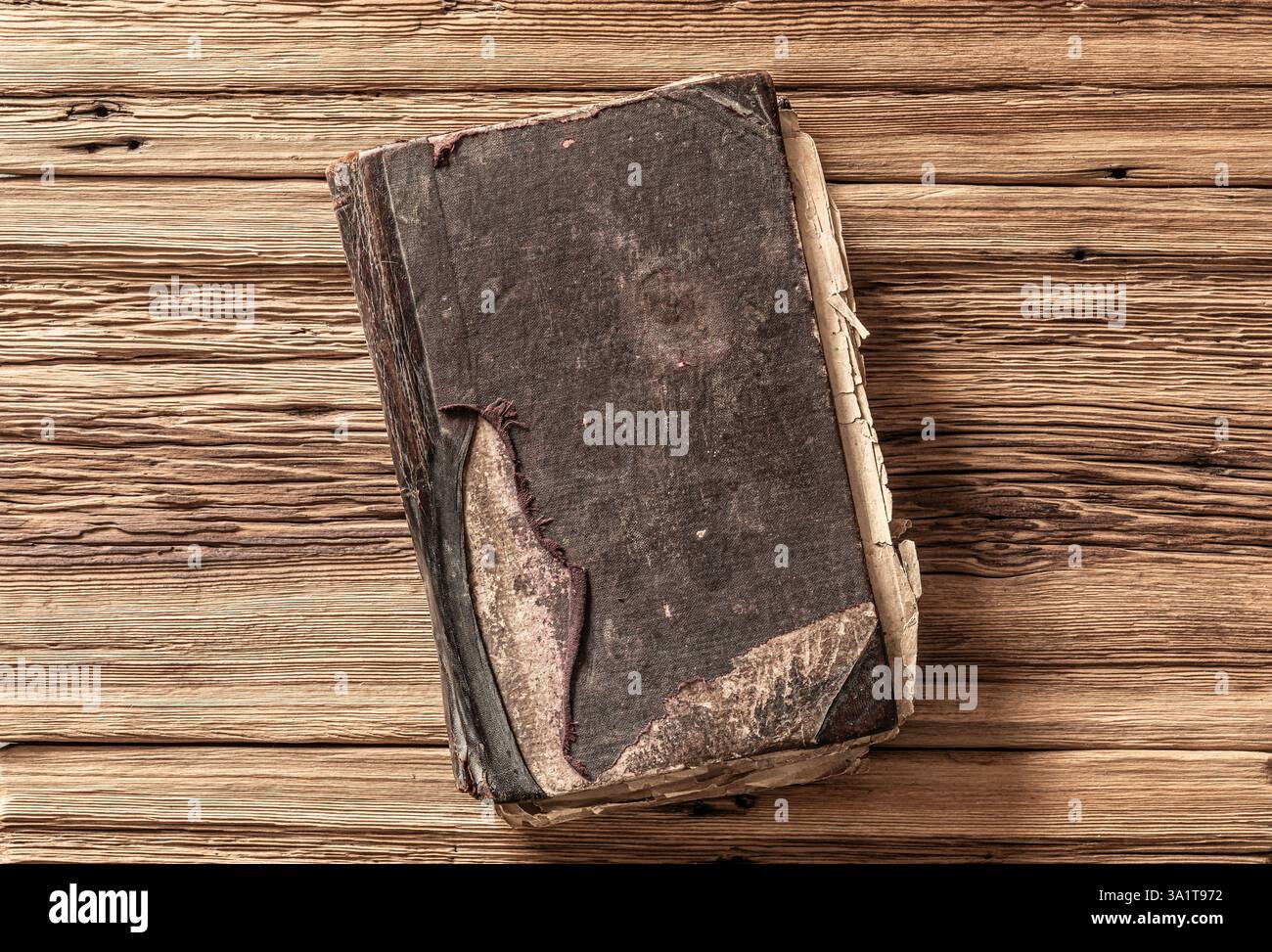 A worn book lies on a textured wooden surface, showcasing its aged ...