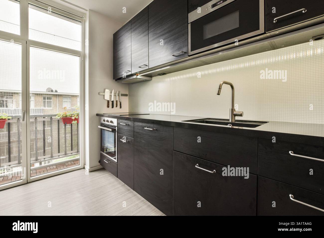 A sleek modern kitchen featuring black cabinetry, stainless appliances, and ample natural light ...