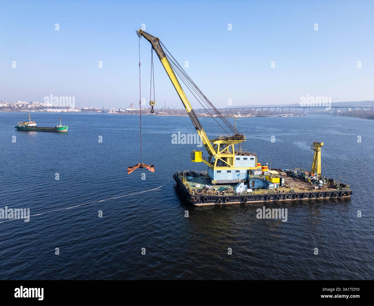 A floating crane barge with a large yellow crane operates on calm ...
