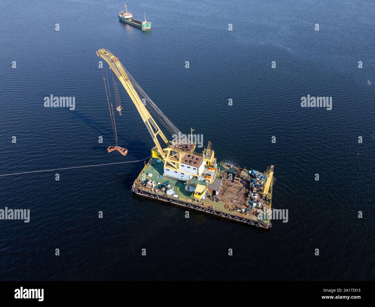 A floating crane barge with a large yellow crane operates on calm ...