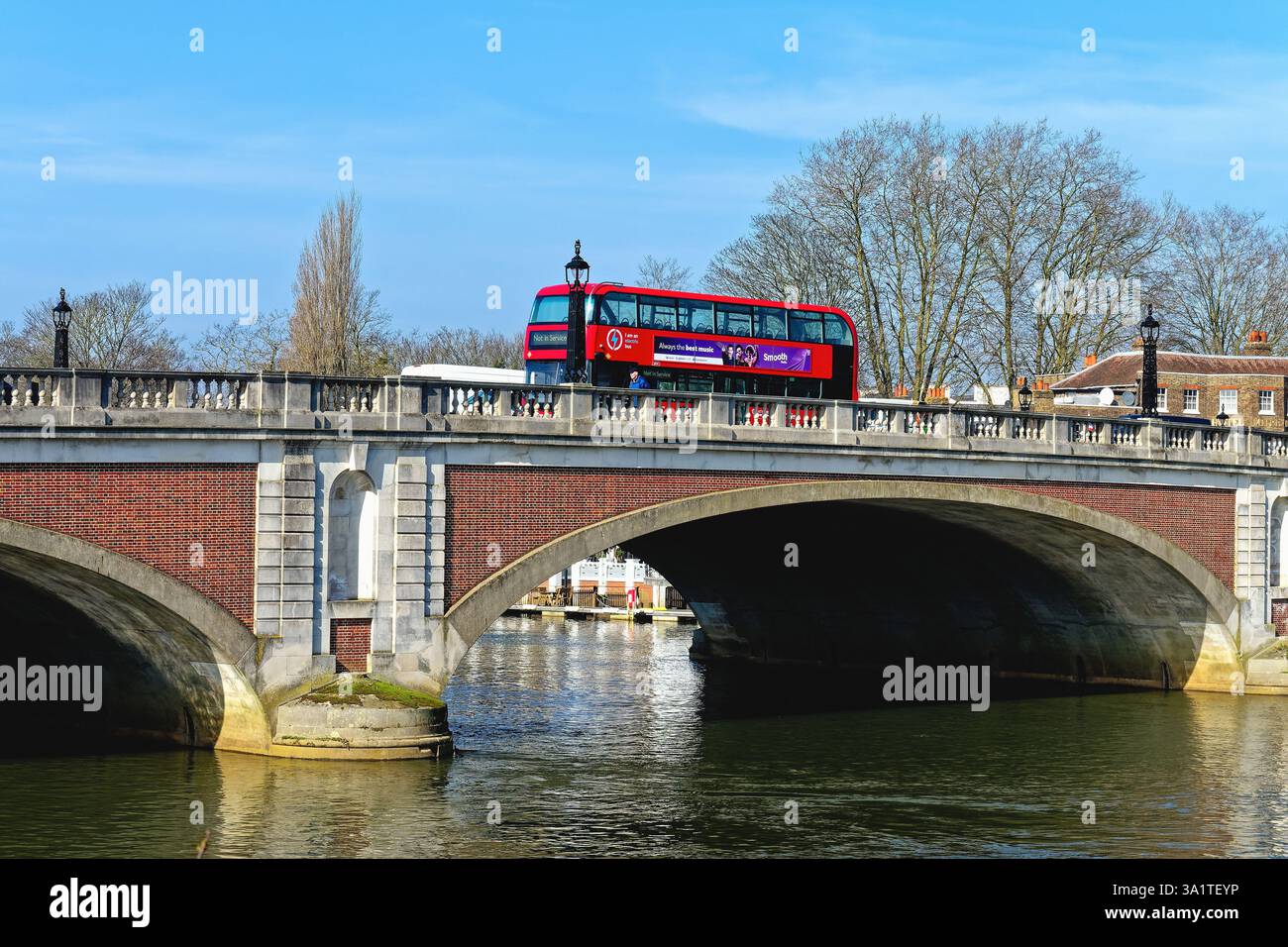 A red London double decker bus crossing over Hampton Court bridge ...