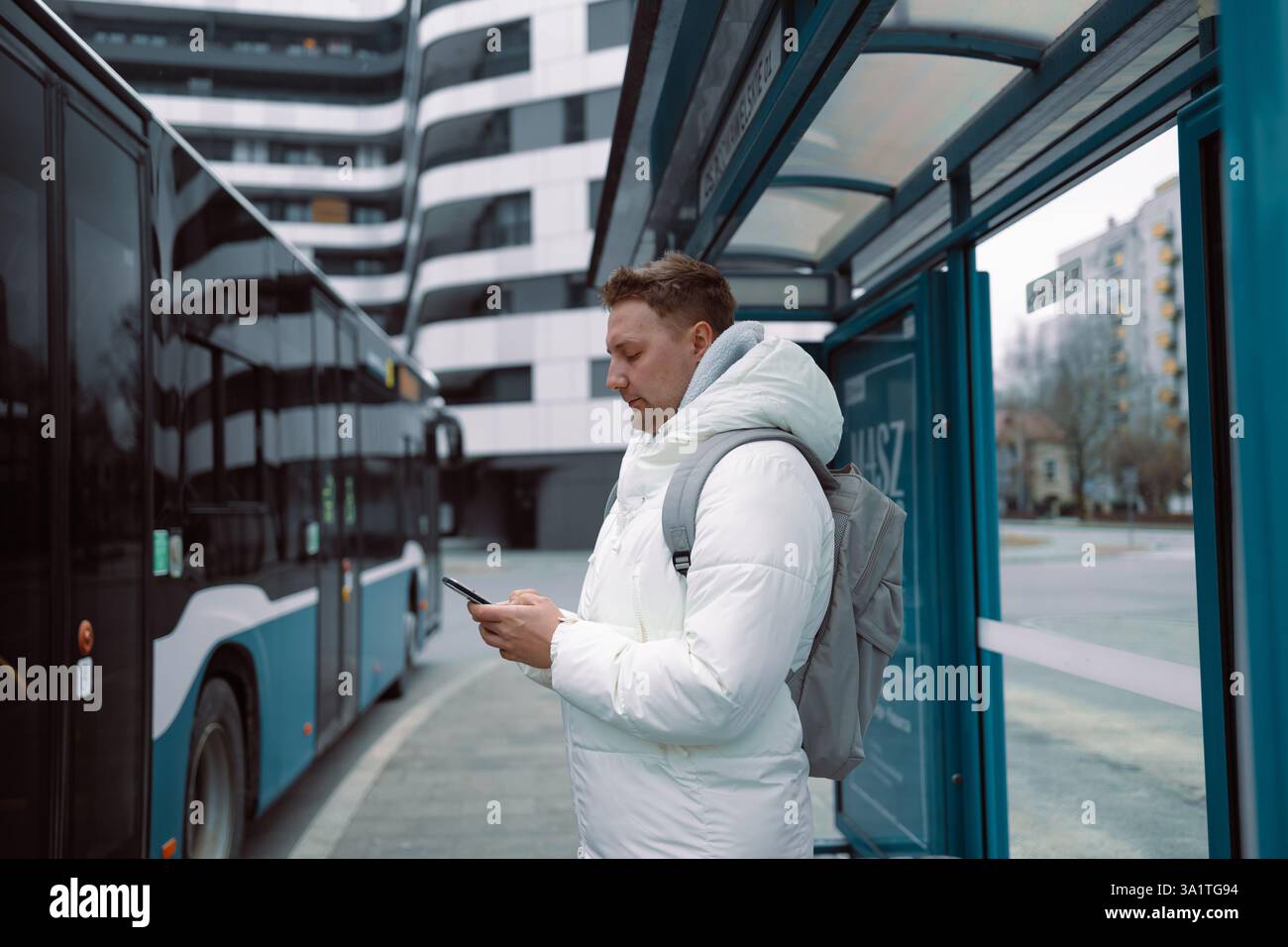 Young stylish man with smart phone on bus stop and typing sms stand at ...
