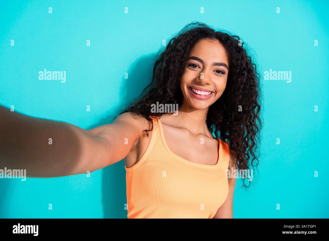 Smiling woman taking a selfie in bright turquoise background, wearing ...