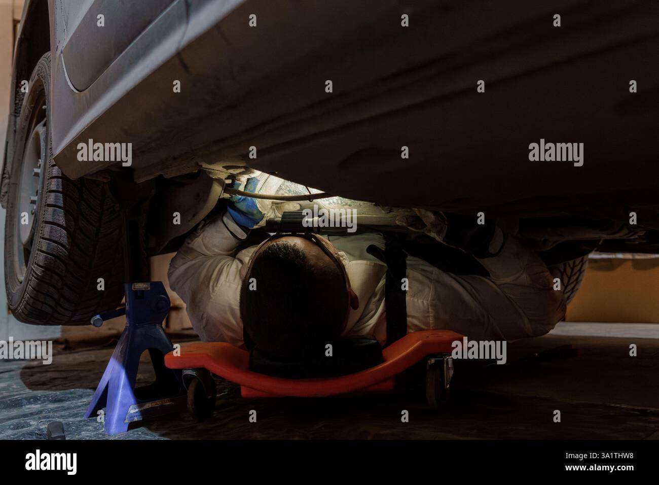 Mechanic lying on creeper inspecting underside of vehicle during ...