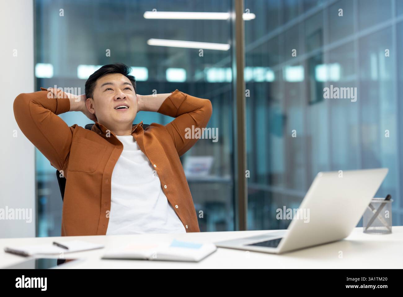 An asian professional man in an office leans back in his chair with ...