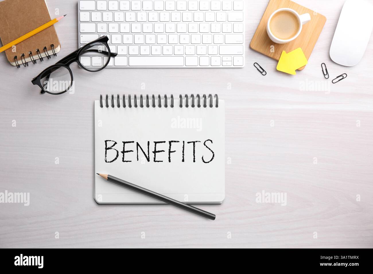 Benefits word in notebook, pencil, eyeglasses, computer keyboard and mouse on white wooden table ...