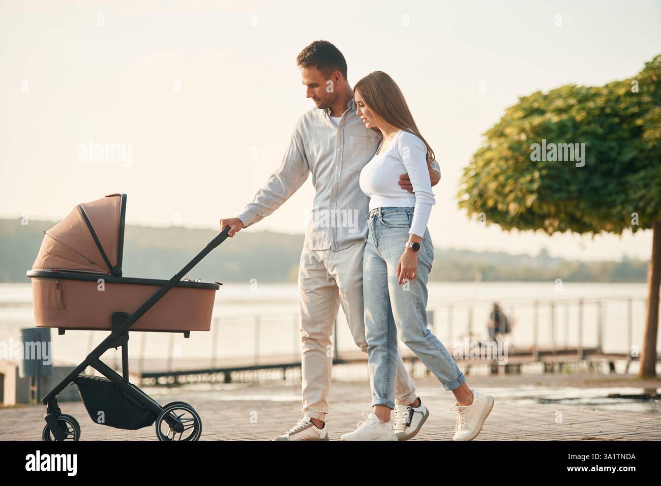 Embracing the woman by the waist. A young couple with a baby pram is ...