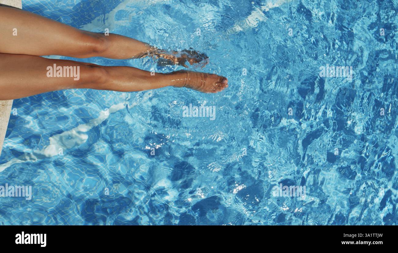 Woman is sitting at the edge of the pool with her legs dangling in the ...