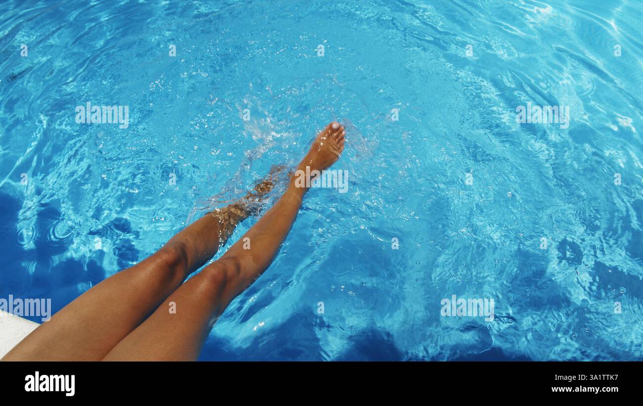 Woman is sitting at the edge of the pool with her legs dangling in the ...
