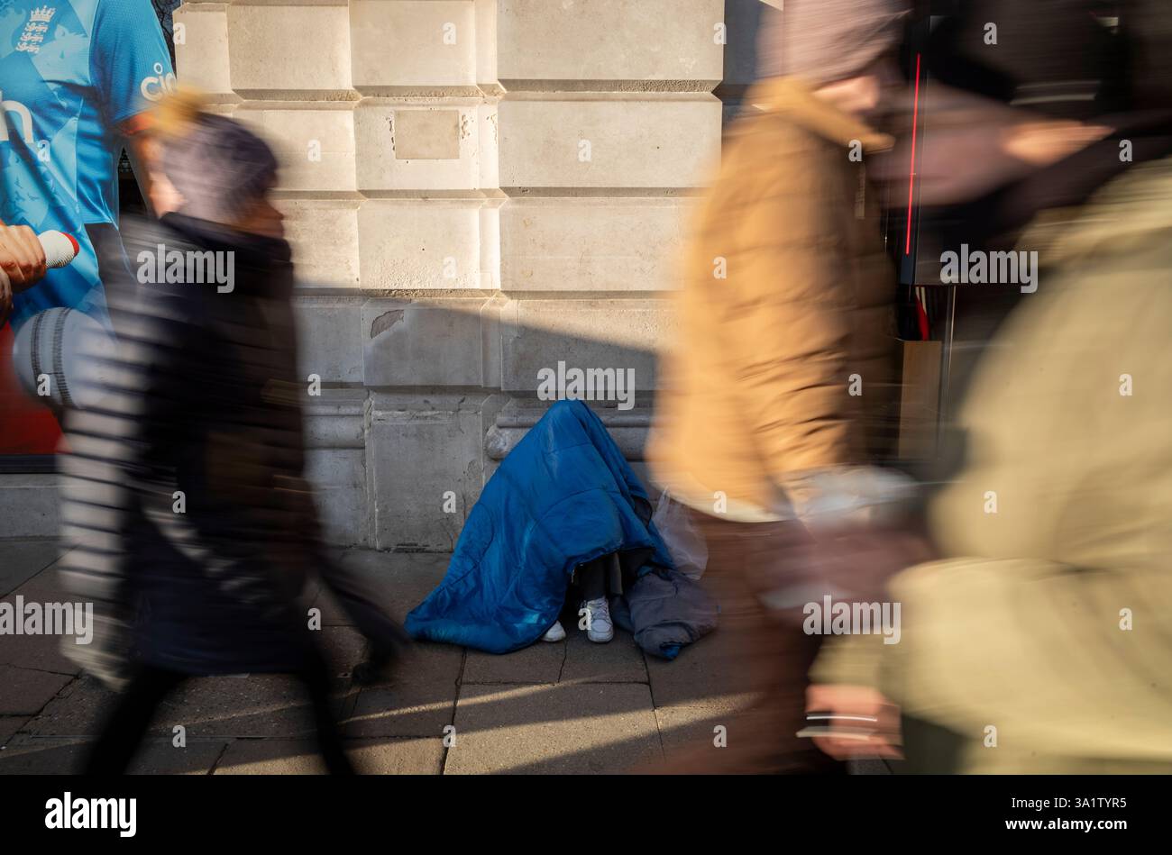 Homeless woman covered by a sleeping bag whilst sat on the pavement ...