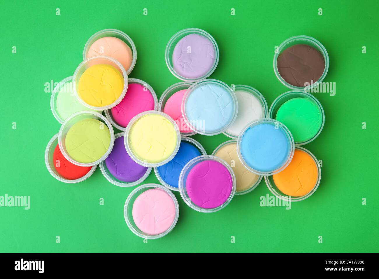 Different colorful modeling clay in plastic jars on green background ...