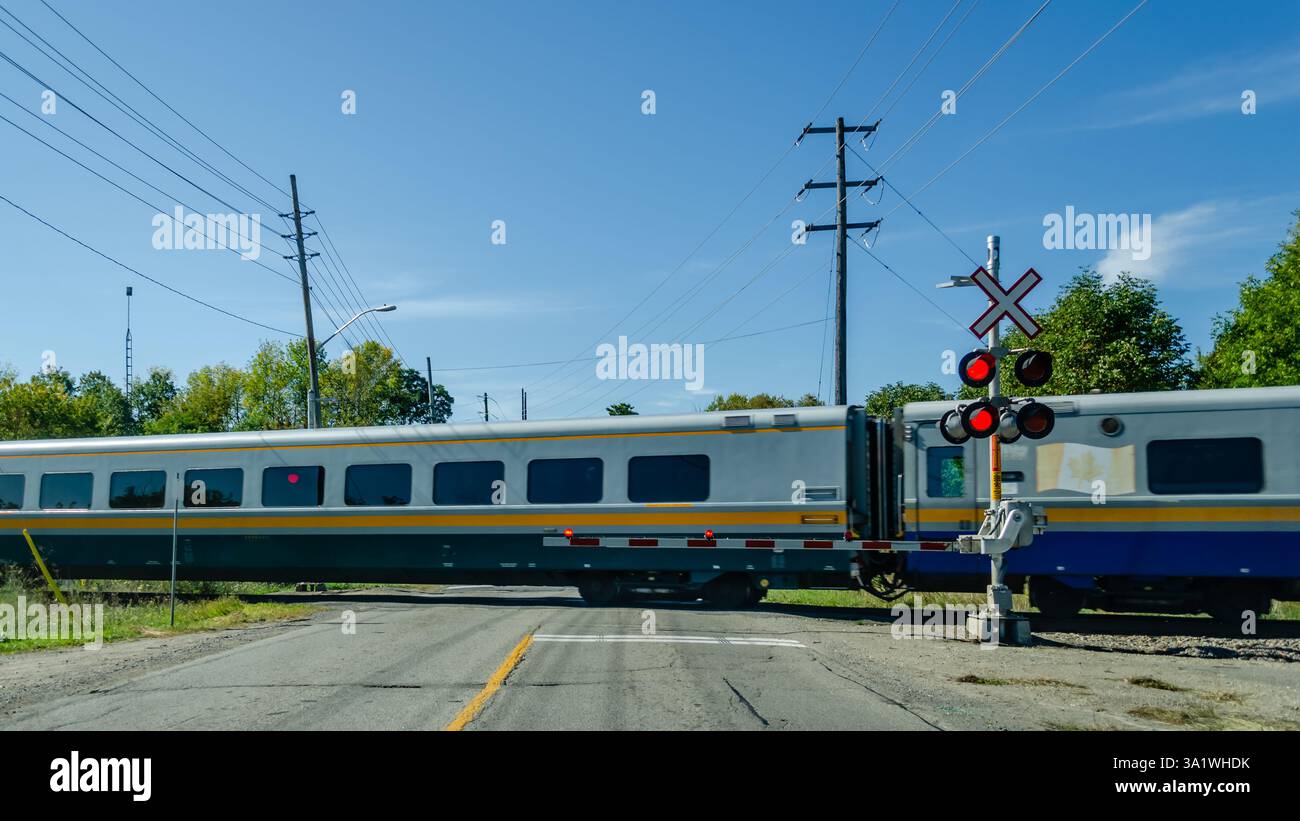 Passenger train cars moving past a level crossing gate on a road in the ...