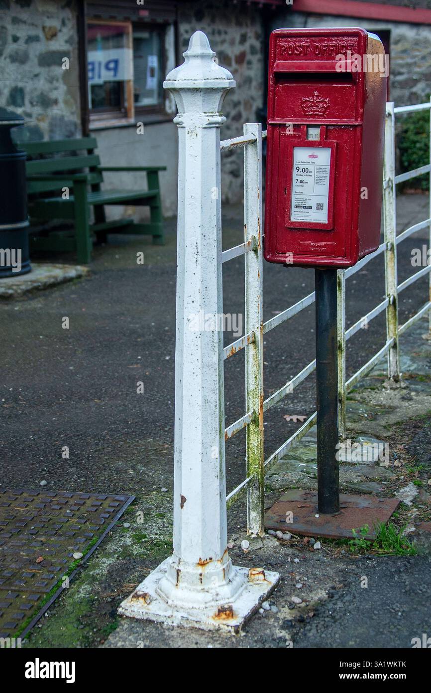 A bright red, British post box on a black pole next to white railings ...