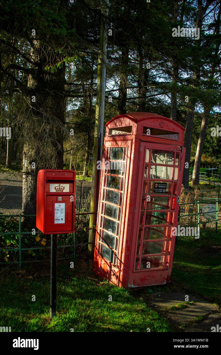 A bright red, British post box on a black pole, by green railings, at ...