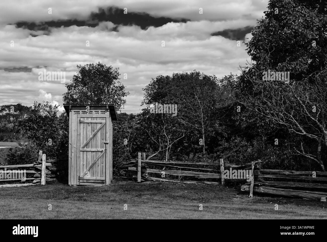 Rustic outhouse next to a split rail fence and trees in Black and white ...