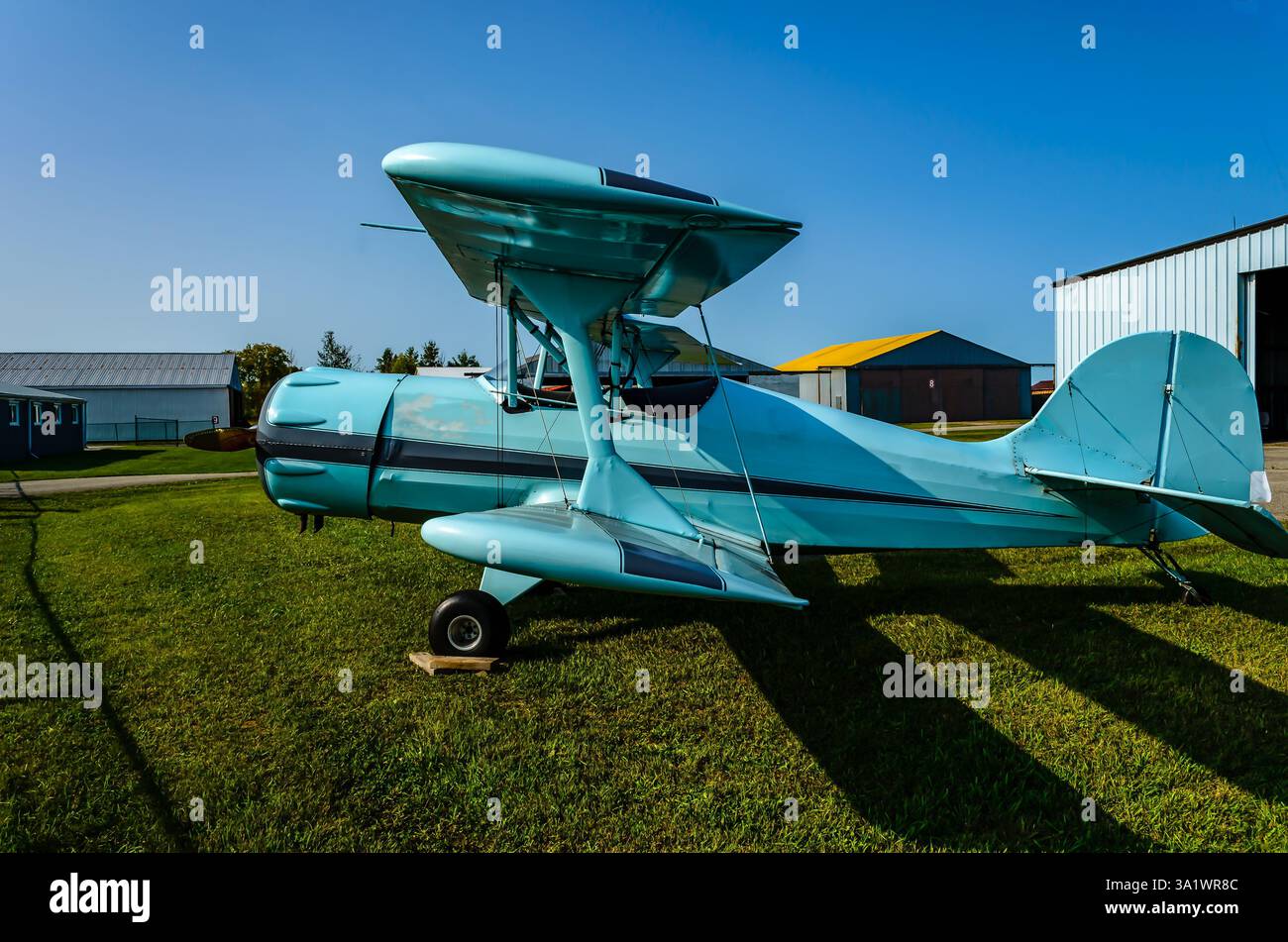 Side view of a Light Blue Bi-Plane parked on the grass outside a set of ...