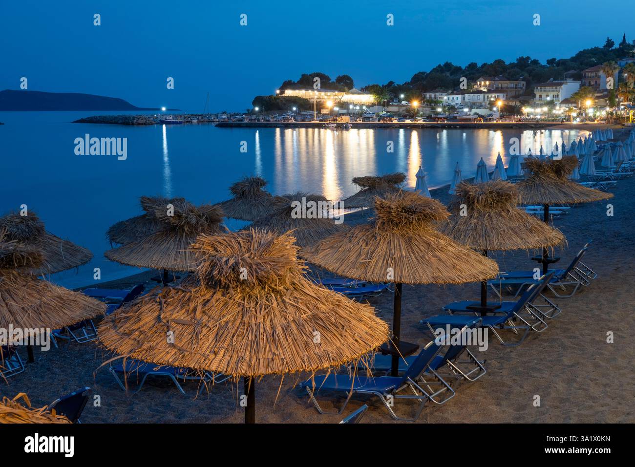 Umbrella lined white sand beach with fishing village behind at night ...