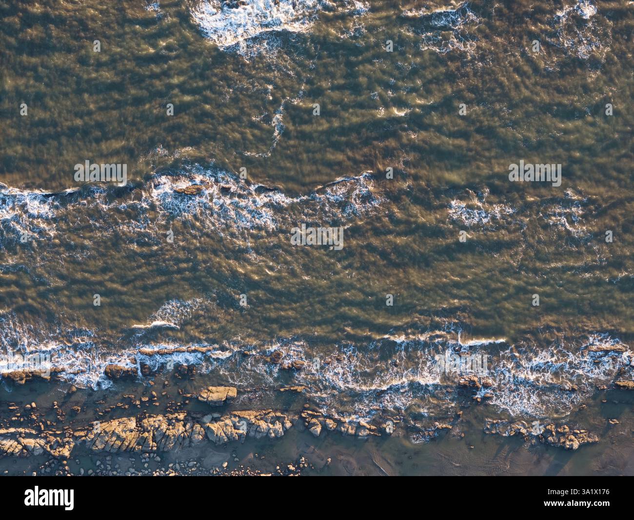 Sunlight casts golden glow on ocean waves as they gently crash against ...