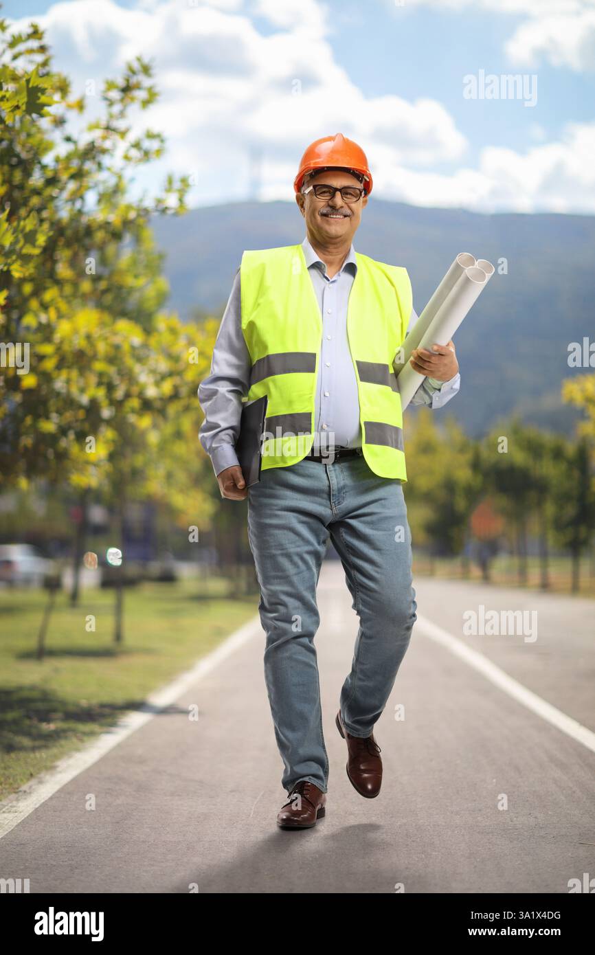 Male engineer holding blueprints and walking in a park Stock Photo - Alamy