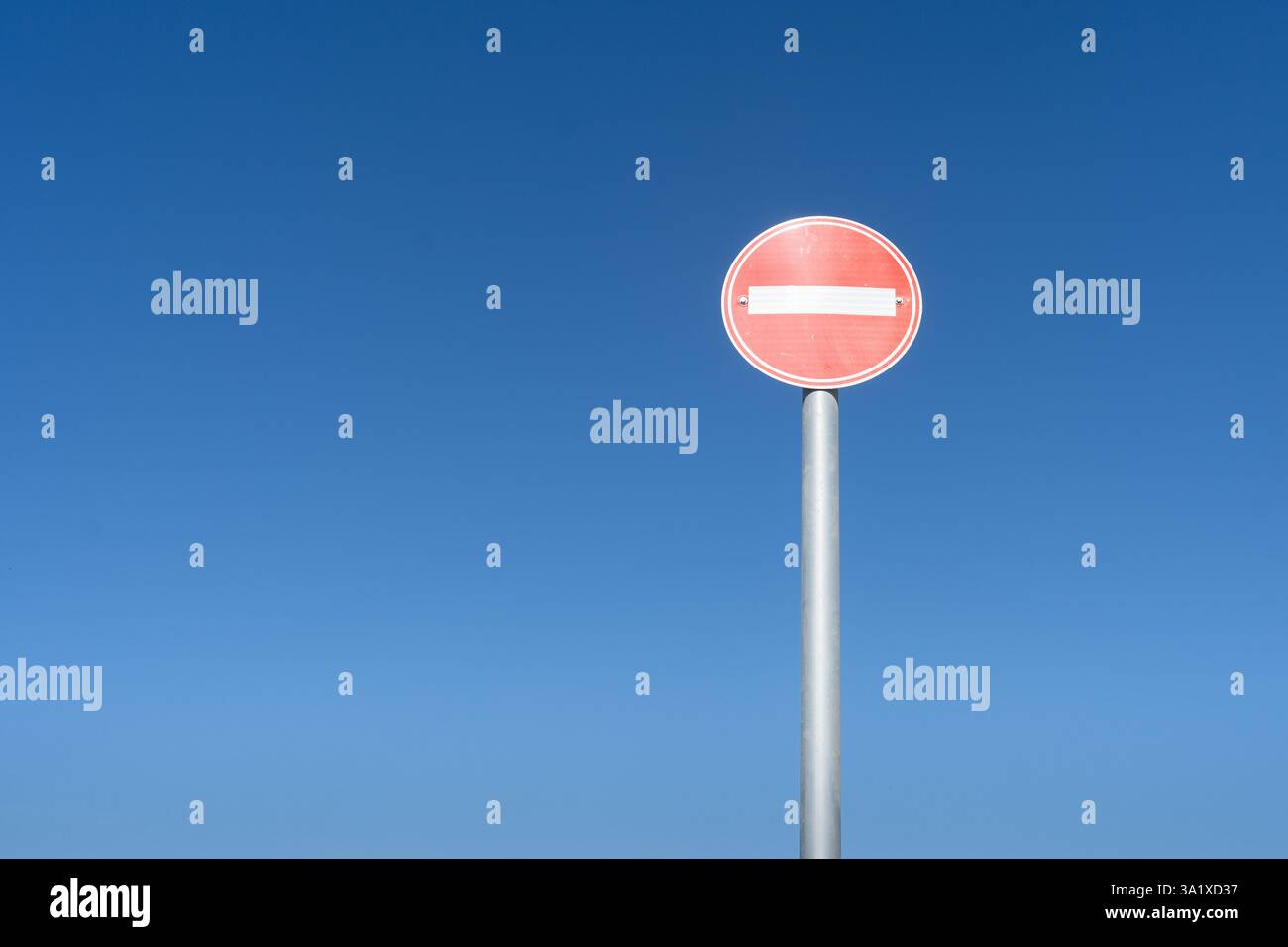 A red no entry traffic sign standing tall against a vibrant blue sky. A ...