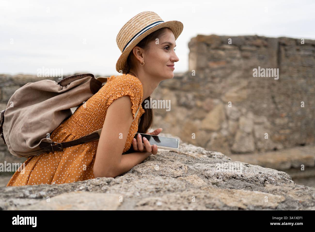 Portrait of female tourist with backpack wearing straw hat looking into ...