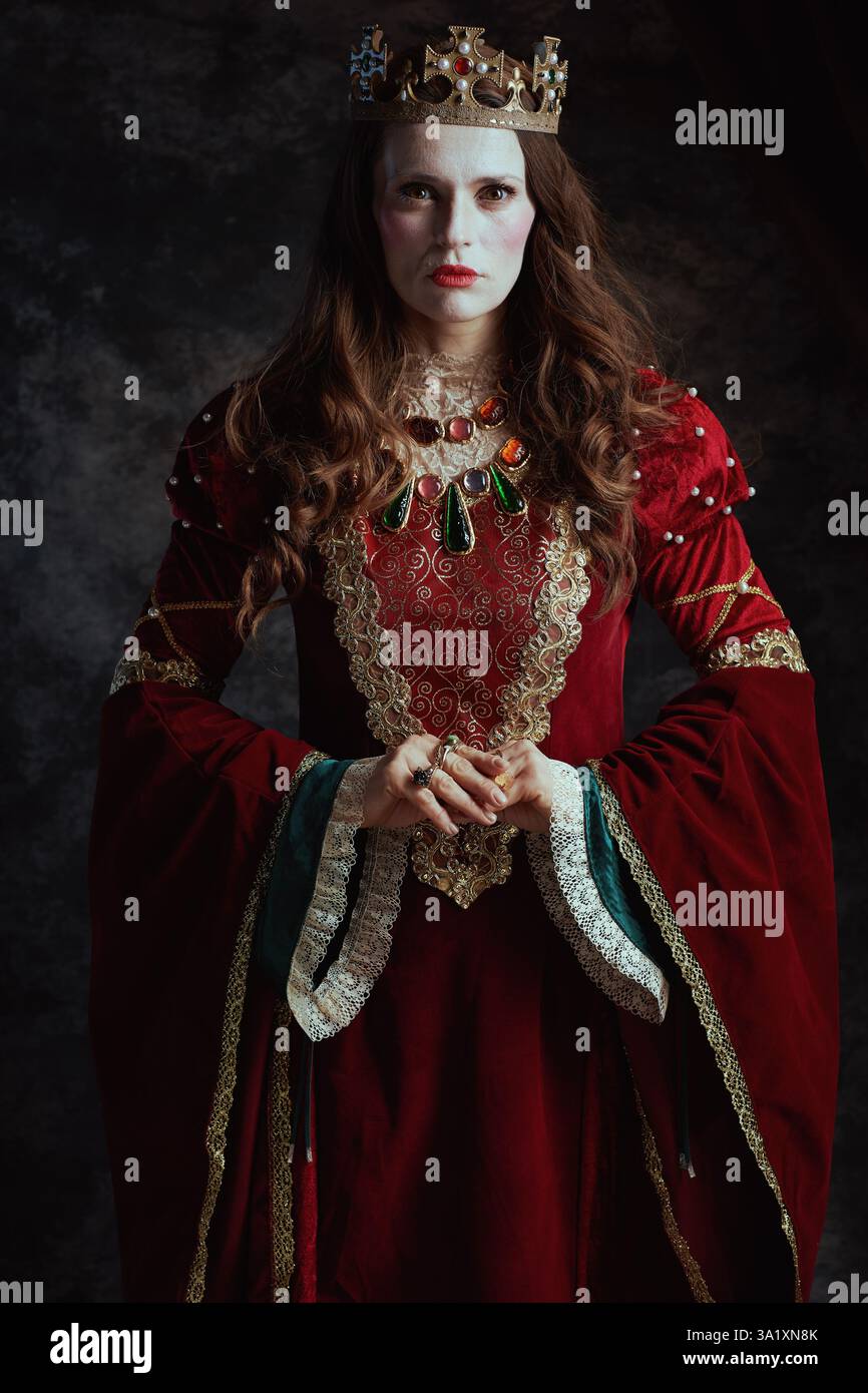 medieval queen in red dress with white makeup and crown on dark gray ...