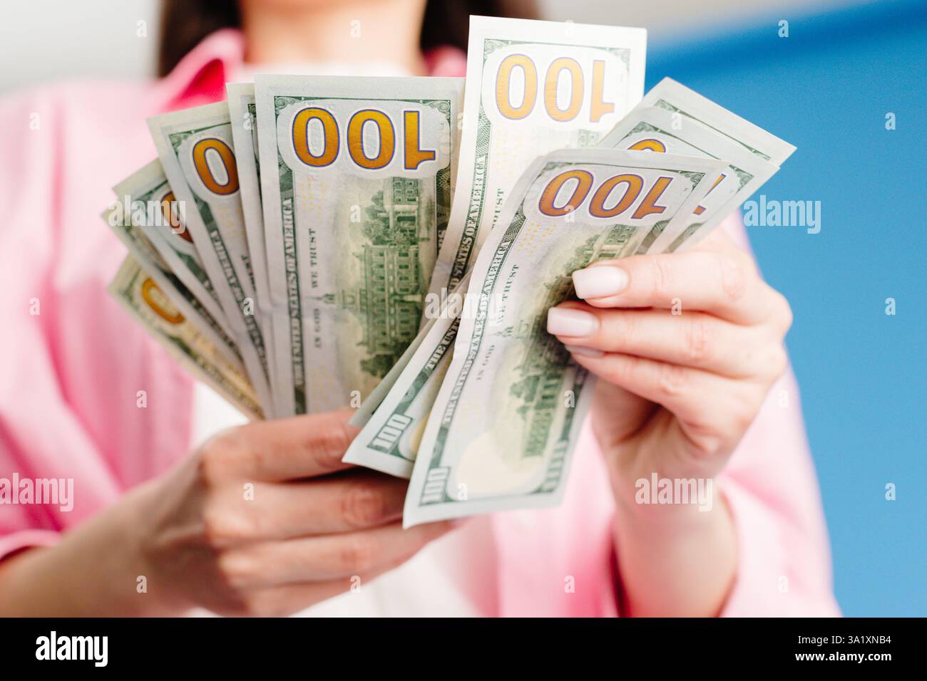 Close-up of female hands counting stack of hundred dollar bills blue background. American money ...