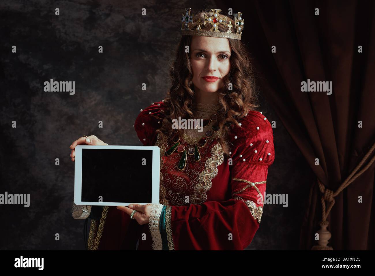 medieval queen in red dress with crown showing tablet PC blank screen ...