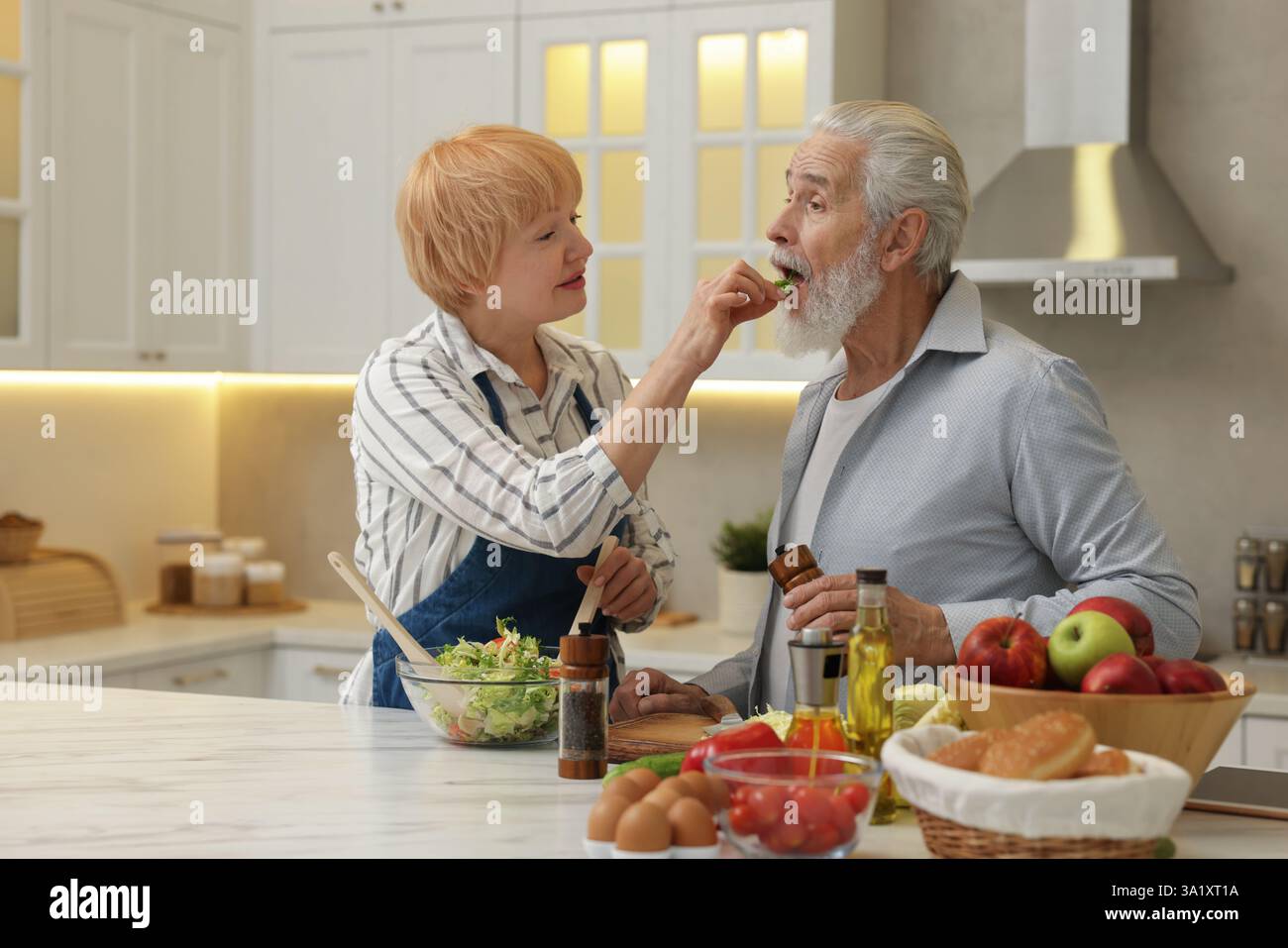 Senior couple feeding each other while cooking in kitchen Stock Photo ...