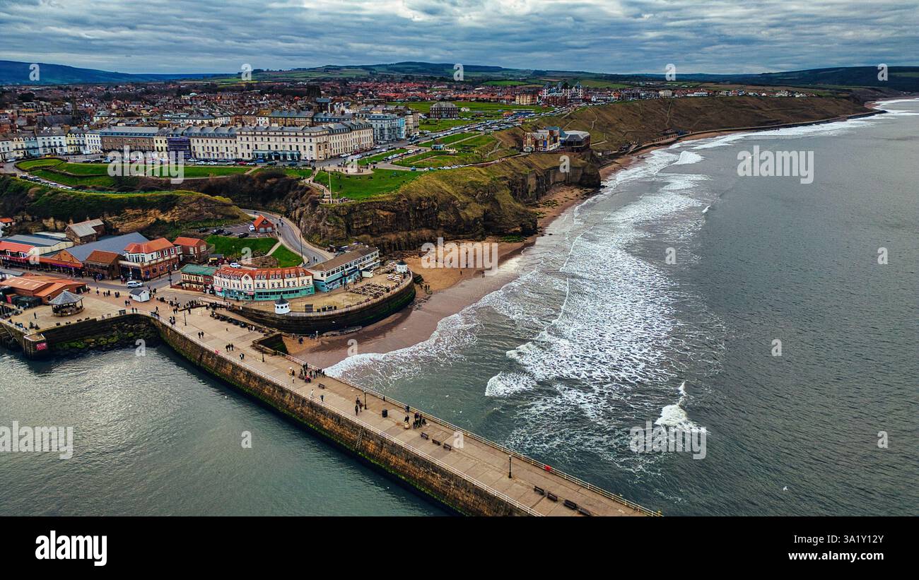 Aerial view of a coastal town featuring a pier, beach, cliffs, and a ...