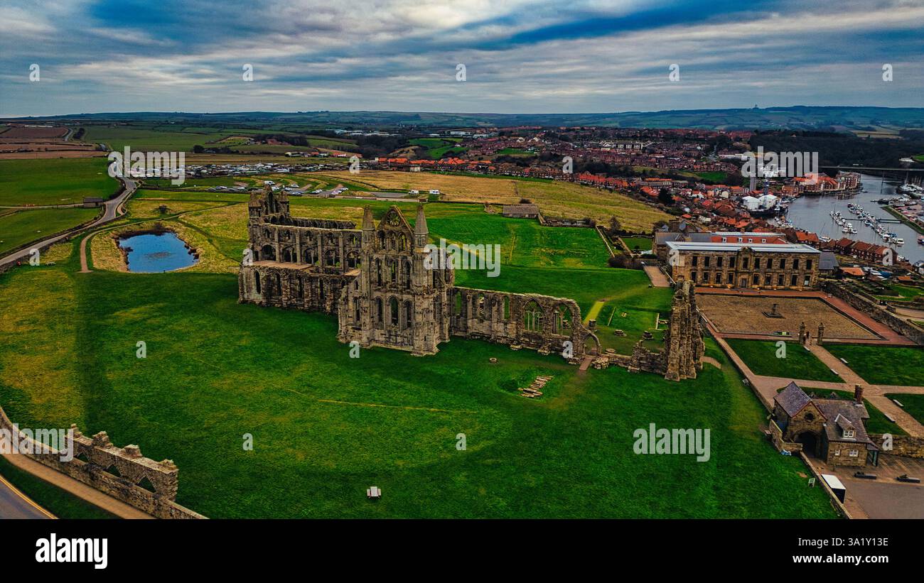 Aerial view of Whitby Abbey ruins surrounded by green fields, a town, a ...