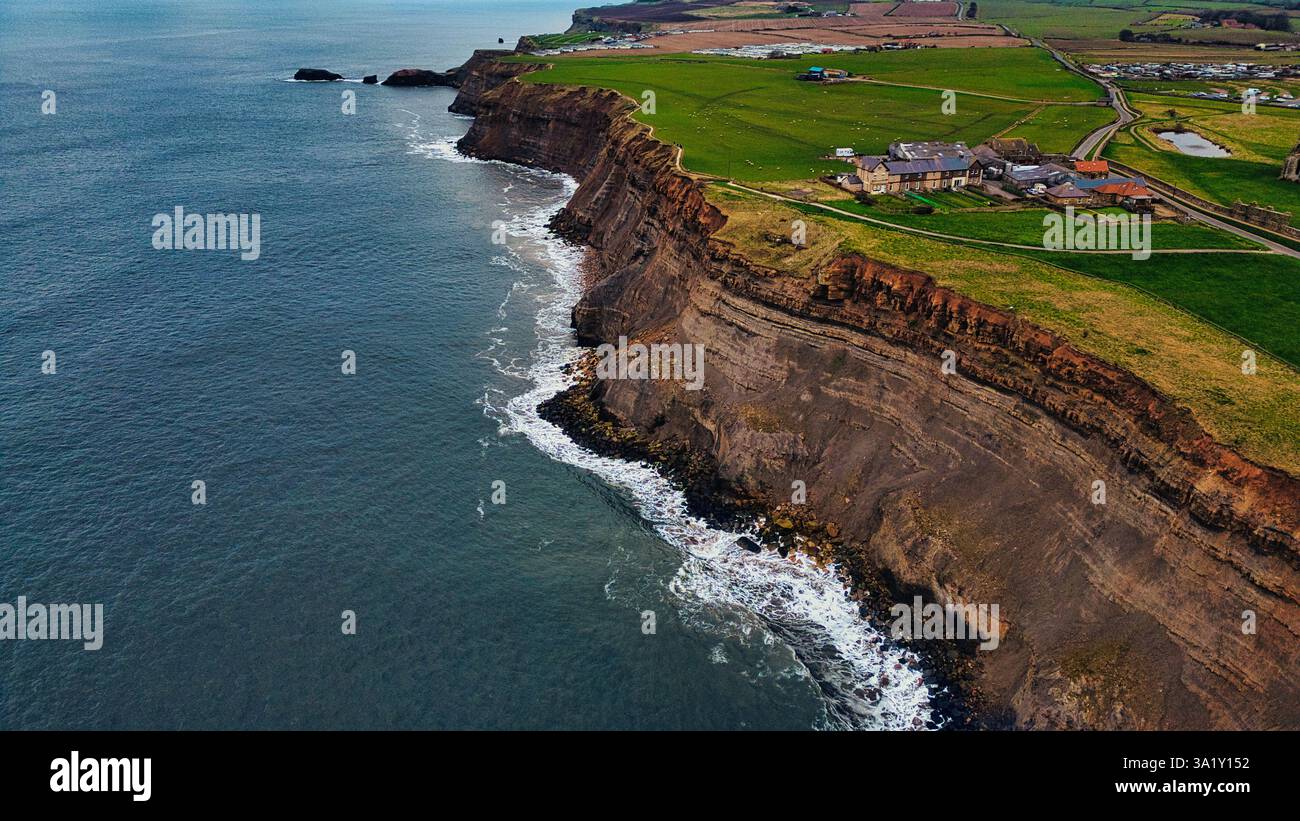 Aerial view of a layered coastal cliff meeting the ocean, topped with ...
