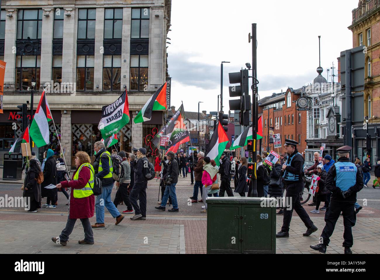 A street scene shows a protest march with Palestinian flags, signs, and ...