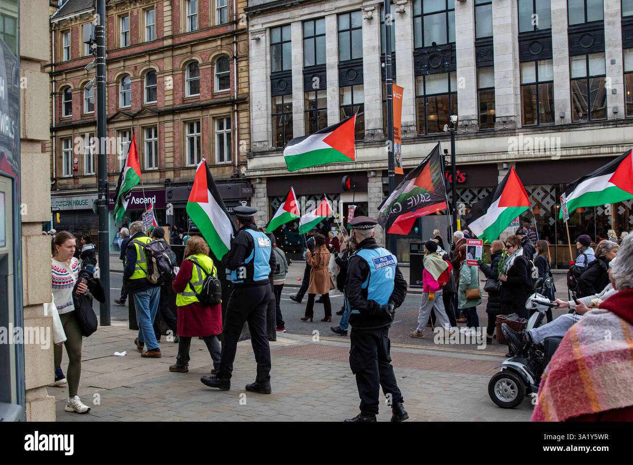 A street scene depicting a protest march with Palestinian flags. Police ...