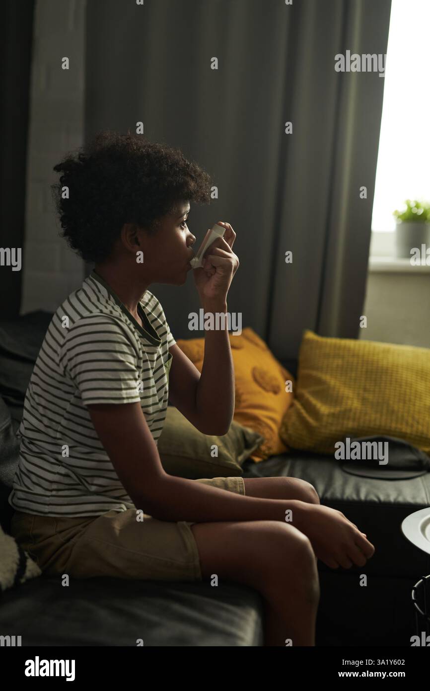 Side view of youngster in casual attire pumping inhaler and inhaling ...